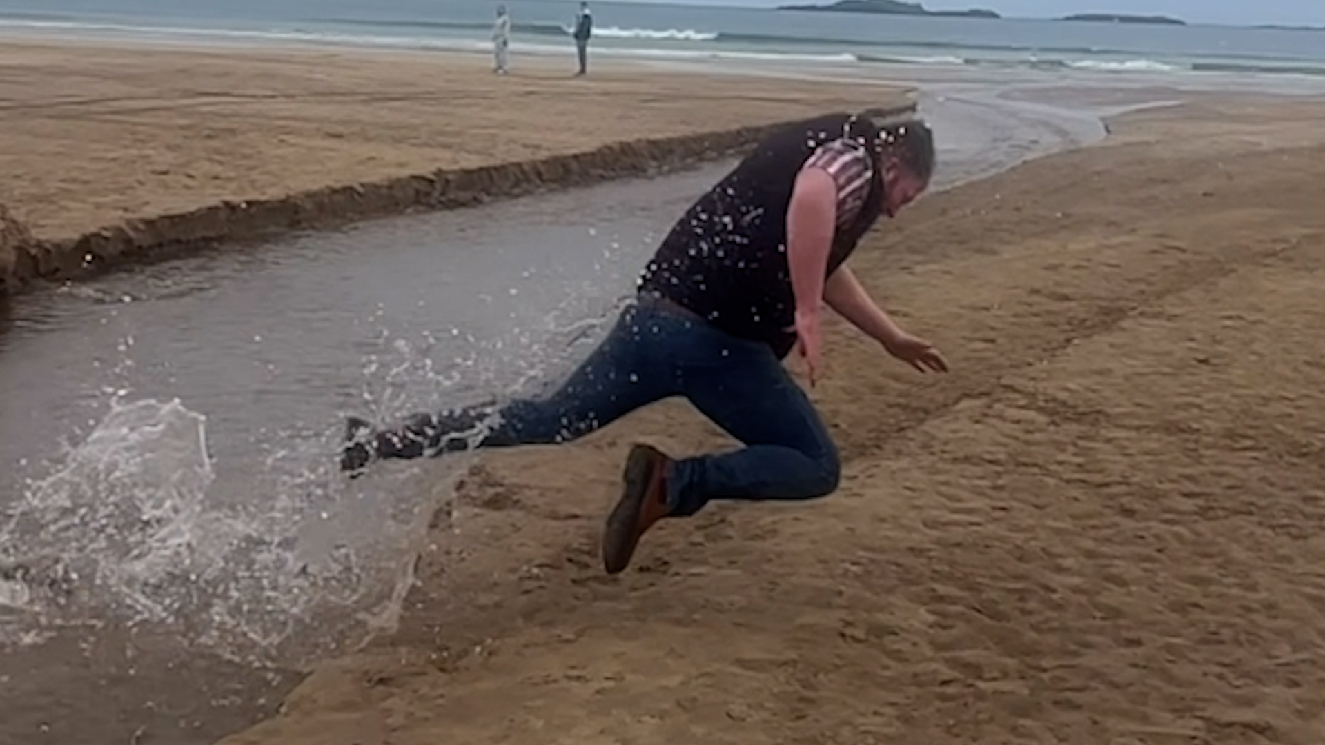 Funny moment man falls short attempting to jump across beach trench