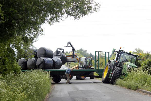 Overturned tractor with load of straw bales blocks village road
