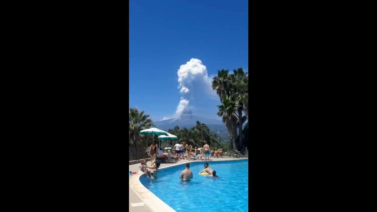Mount Etna ash cloud towers above tourists in swimming pool