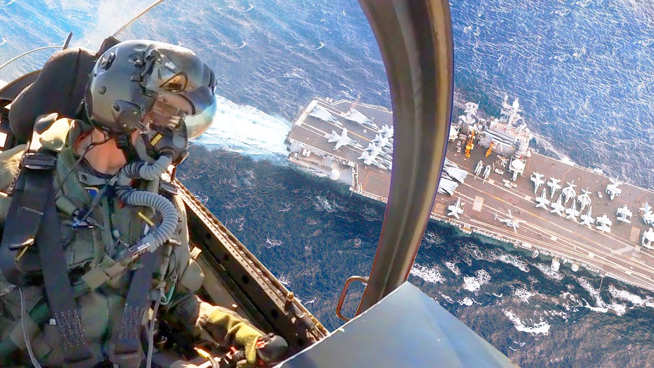 Navy jets soar at low altitude over the deck of an aircraft carrier