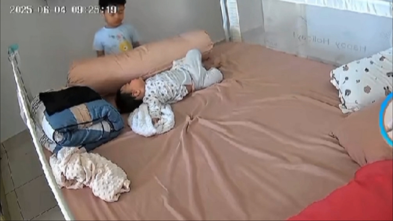 Big brother watches over baby sister in bed while mom tidies up in ...