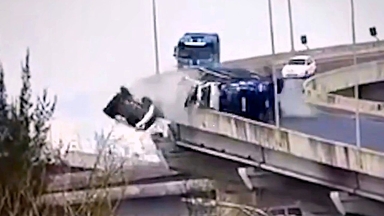 Car transporter truck overturns and sends brand-new car flying off bridge