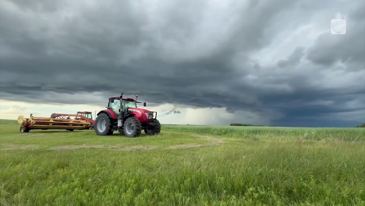 A farm tractor sits in a field with very dark storm clouds hanging overhead