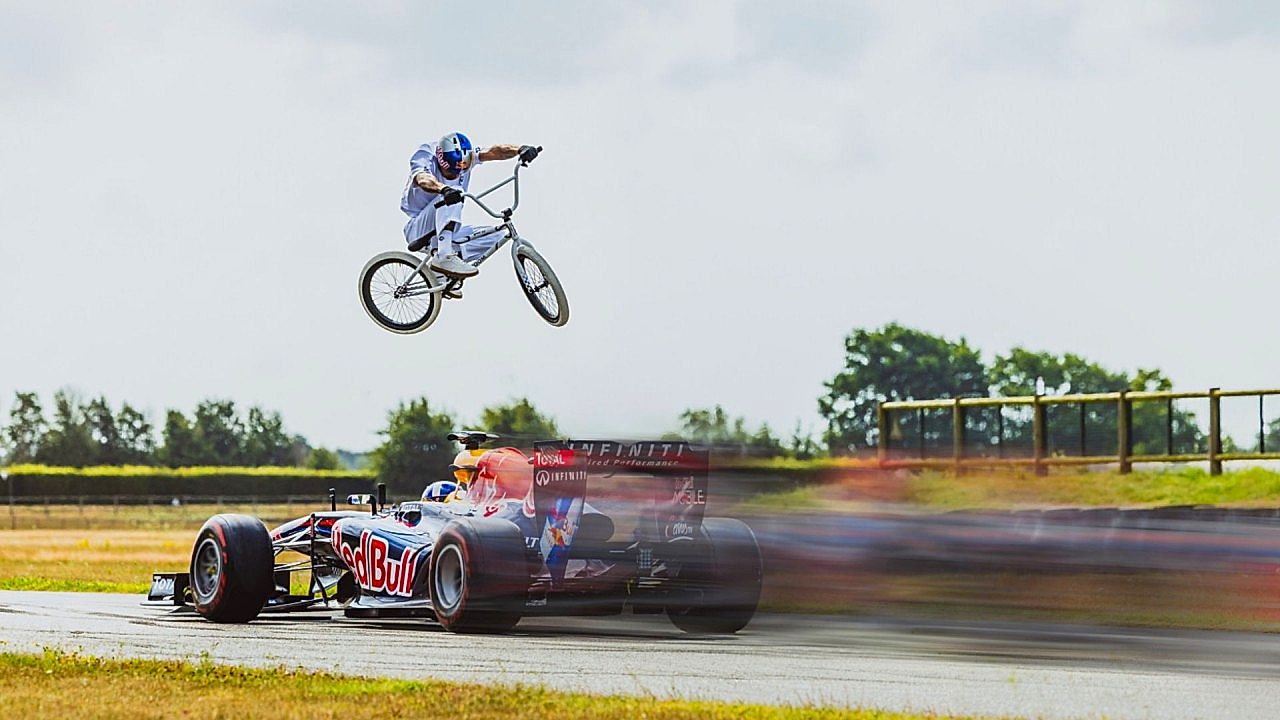 Daredevil BMX rider bunny hops over moving Formula 1 car