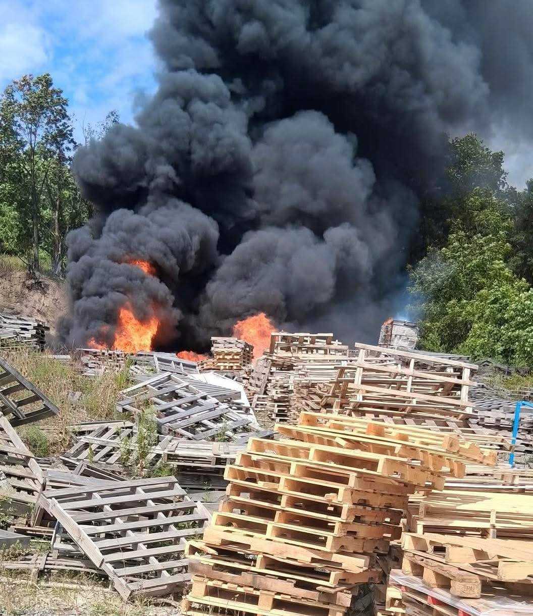 Black smoke billows from large field of burning pallets