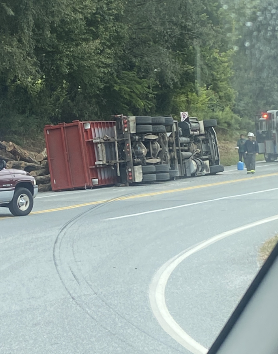 Tractor-trailer carrying logs overturns, blocks road