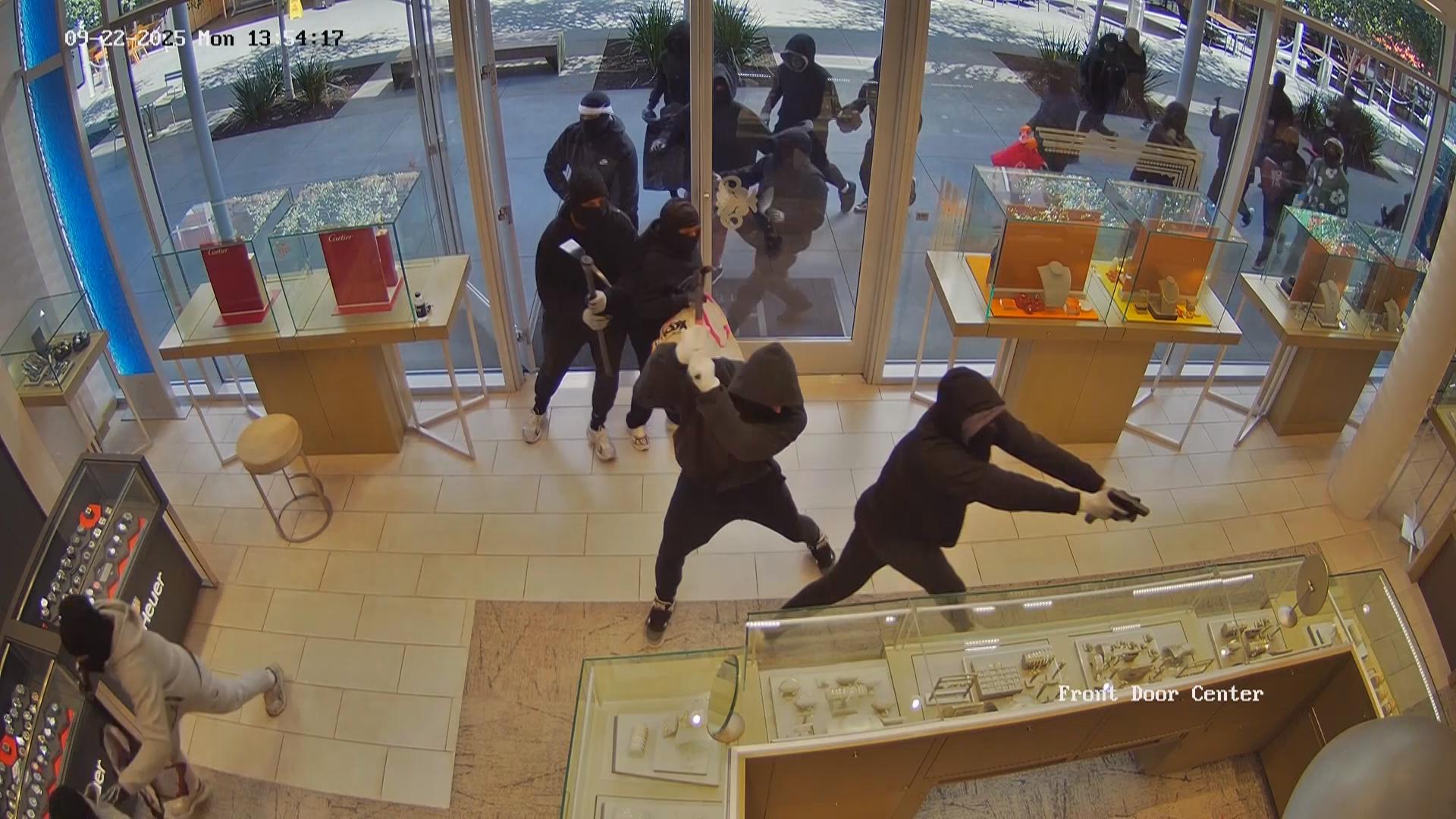 Two dozen people wearing masks and some carrying pickaxes smash jewelry ...
