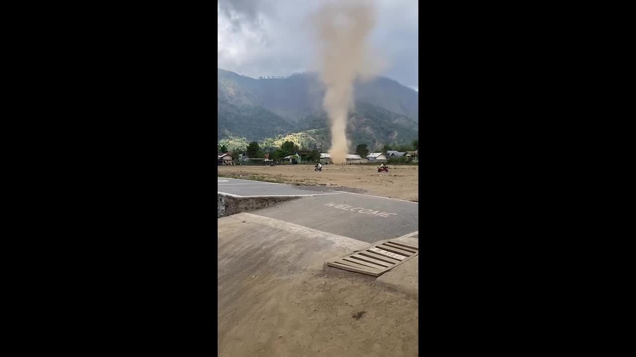 Fearless school children play in dust devil tornado tearing through field
