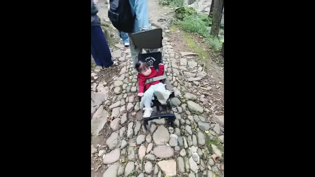 Child endures bumpy stroller ride on rocky path in Zhejiang, China