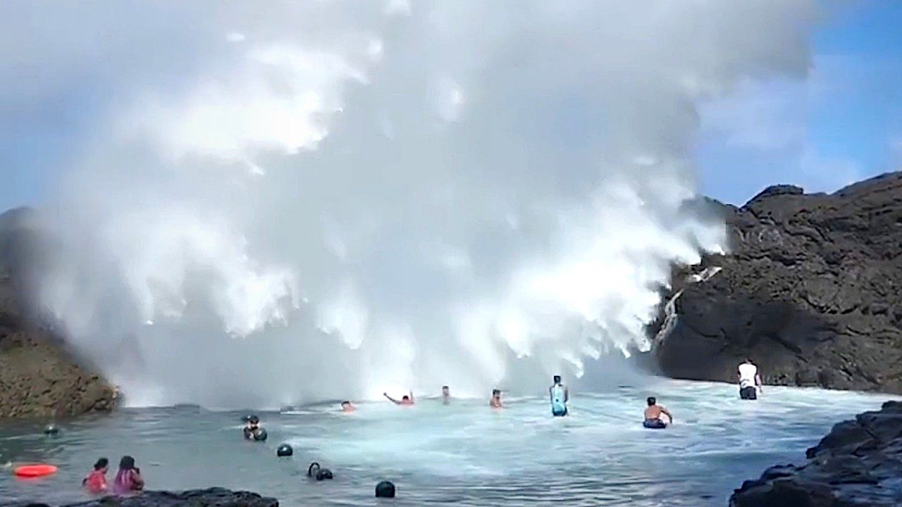 Tourists play in lagoon as 60ft high waves crash onto rocks in the ...