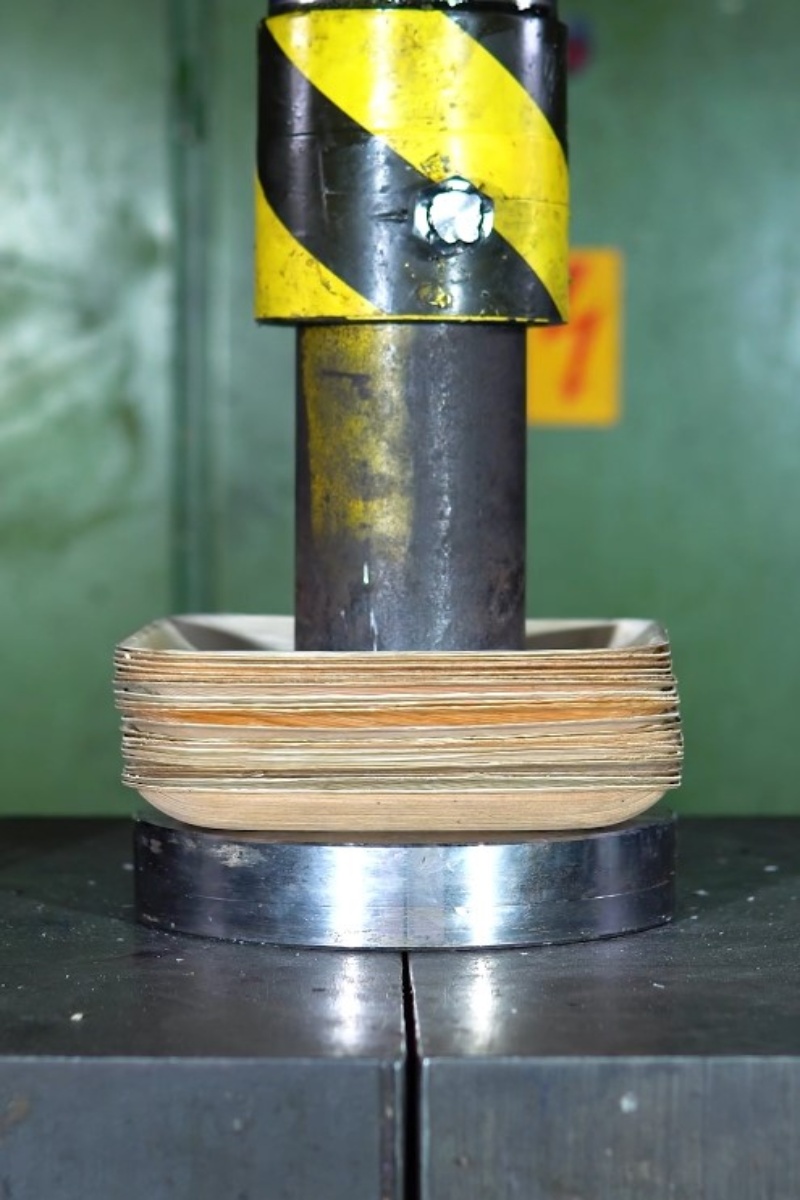 Stack of wooden plates gets flattened by hydraulic press