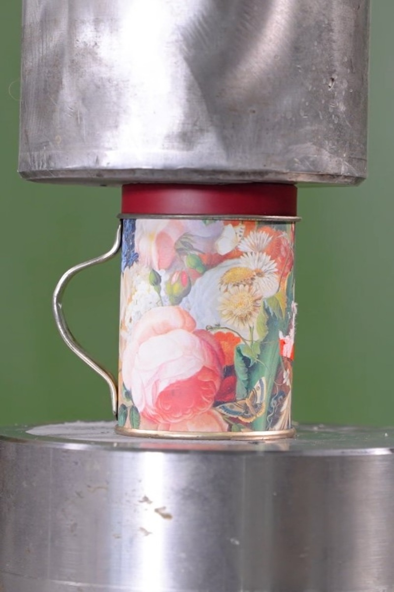 Frantumazione di una coppa di metallo floreale sotto una pressa idraulica