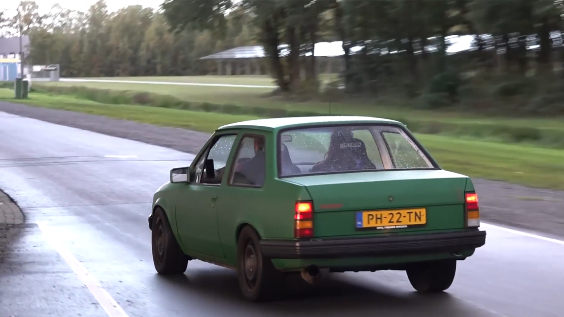 Small green car driving on a wet road after rain