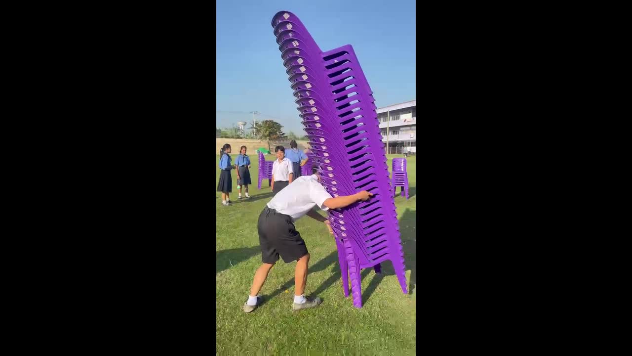 Schoolboy carries huge stack of chairs across field