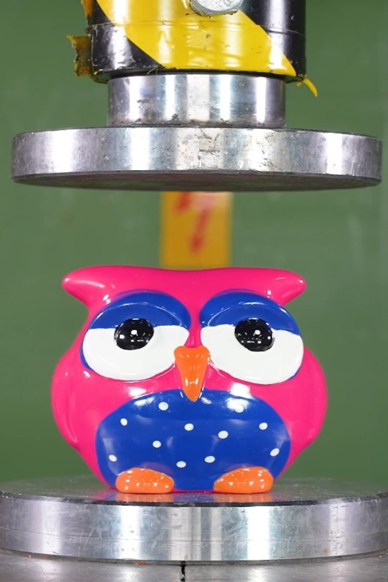 Zgniatanie kolorowej zabawki sowy pod prasą hydrauliczną