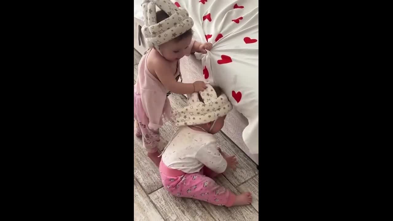 Twin babies playfully tussle with helmets in Simferopol, Russia
