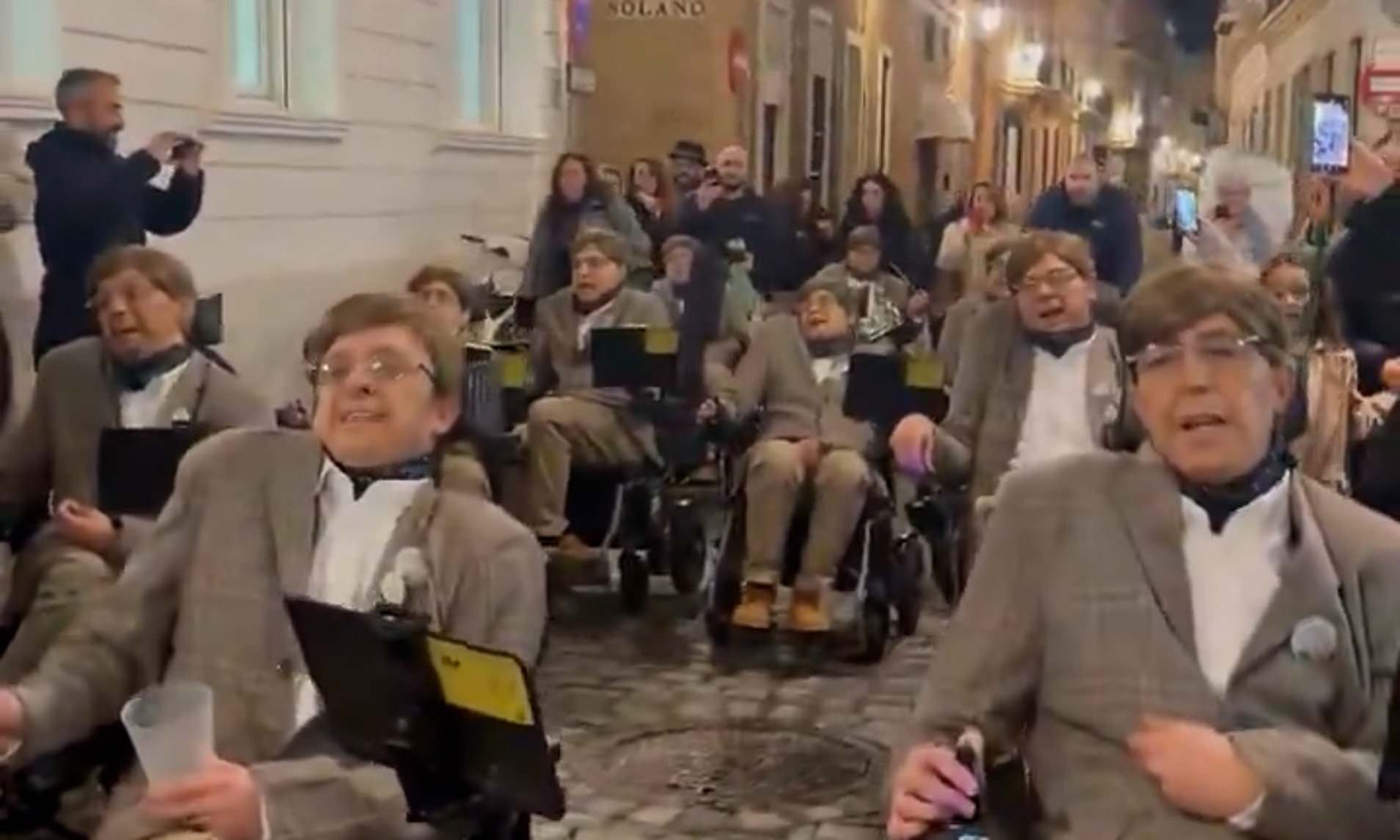 Performers dressed as Stephen Hawking parade and sing in his robotic ...