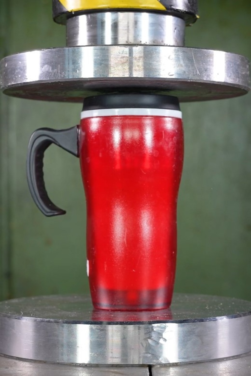 Red travel mug gets crushed under hydraulic press