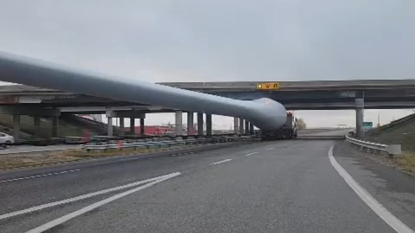 Oversized truck hauls a wind turbine blade under a low bridge