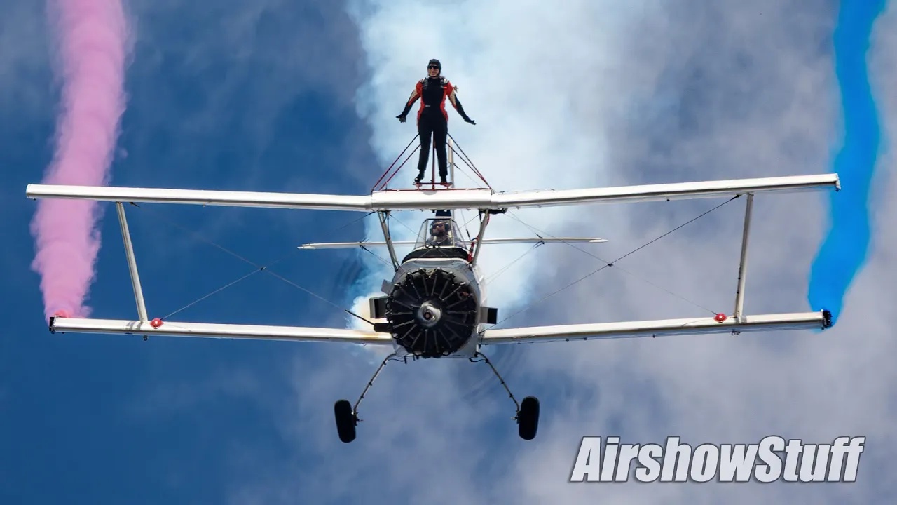 This man is standing on a flying plane while it flips over the crowd!