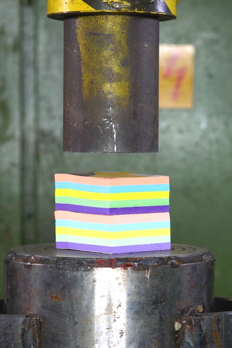 Hydraulische Presse zerdrückt Stapel von farbigem Papier