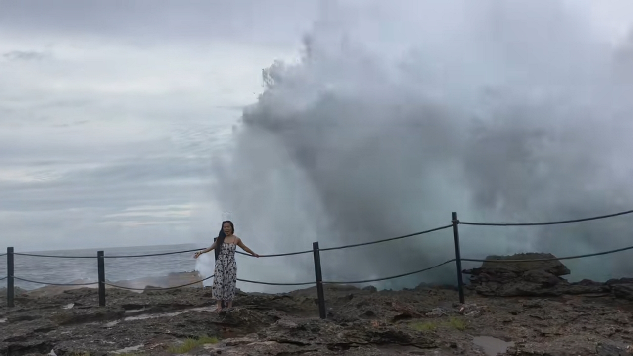 Woman gets splashed by wave on rocky shore in Lembongan Island, Bali ...