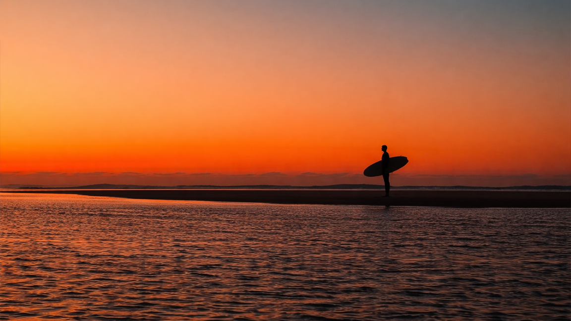 Surfista parado enquanto o horizonte brilha ao anoitecer