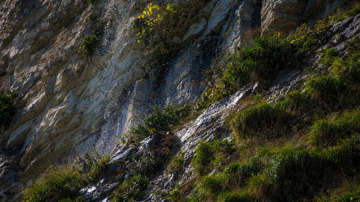 Hidden waterfall flowing down a rocky cliff surrounded by greenery