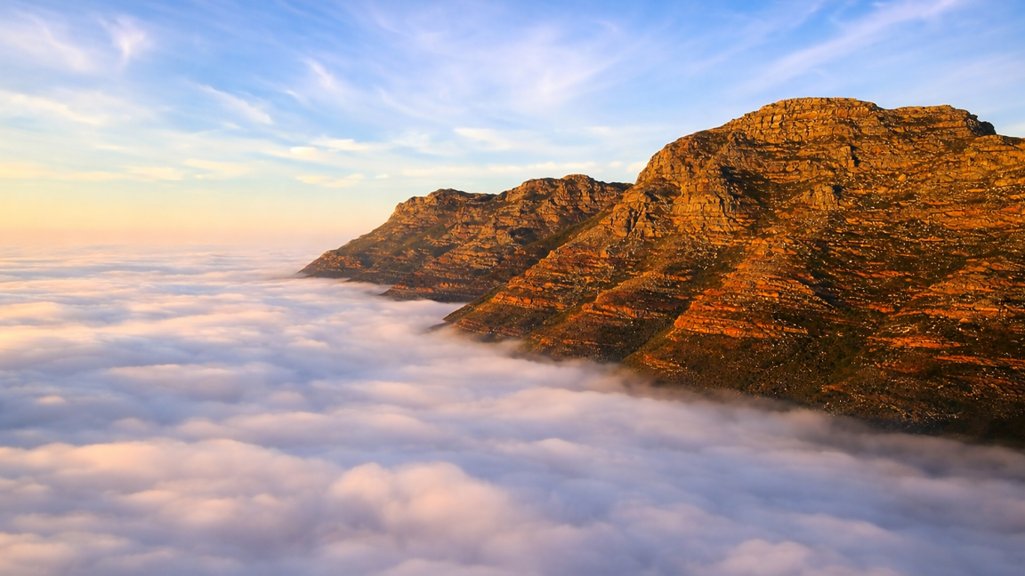 Golden mountain rising above soft sea of clouds at sunrise
