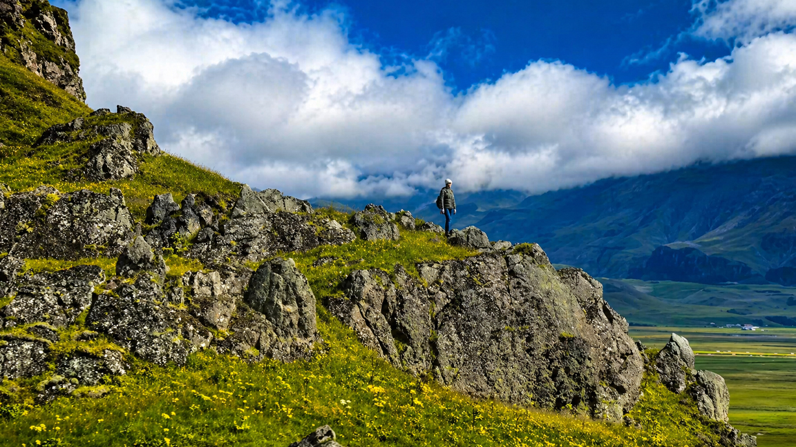 Adventurer on cliff surrounded by green hills and clouds