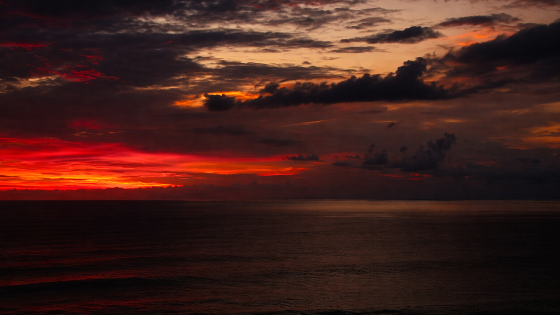 Dramatic sunset over calm ocean with deep red tones