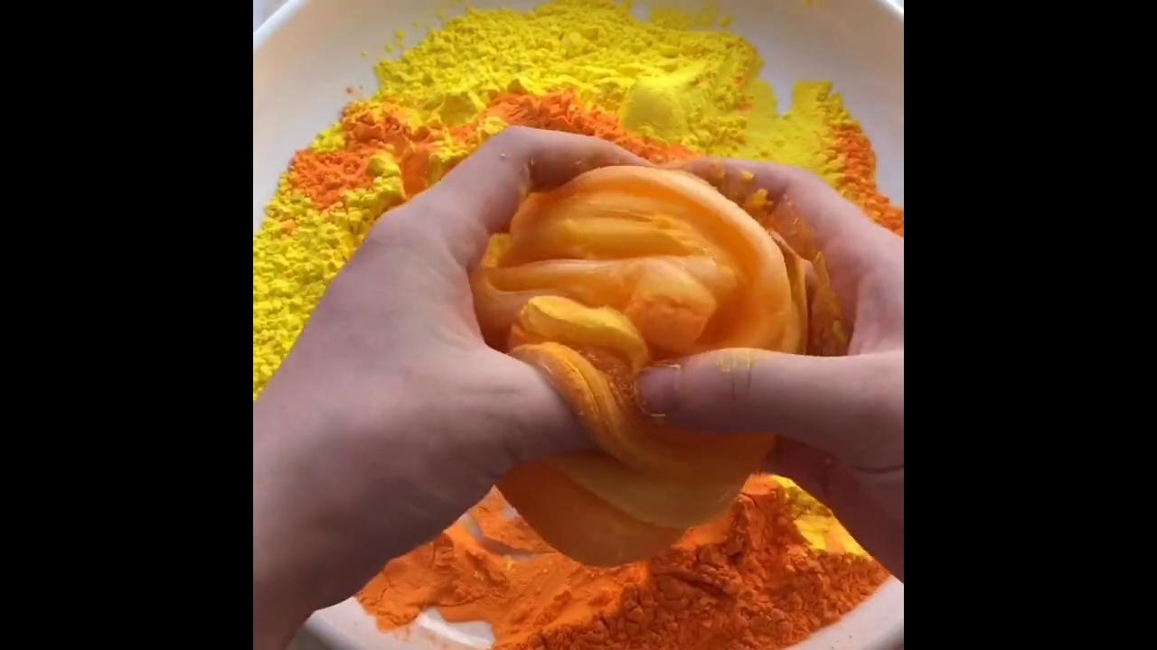 Pulling and folding orange slime into yellow powder producing vibrant ...