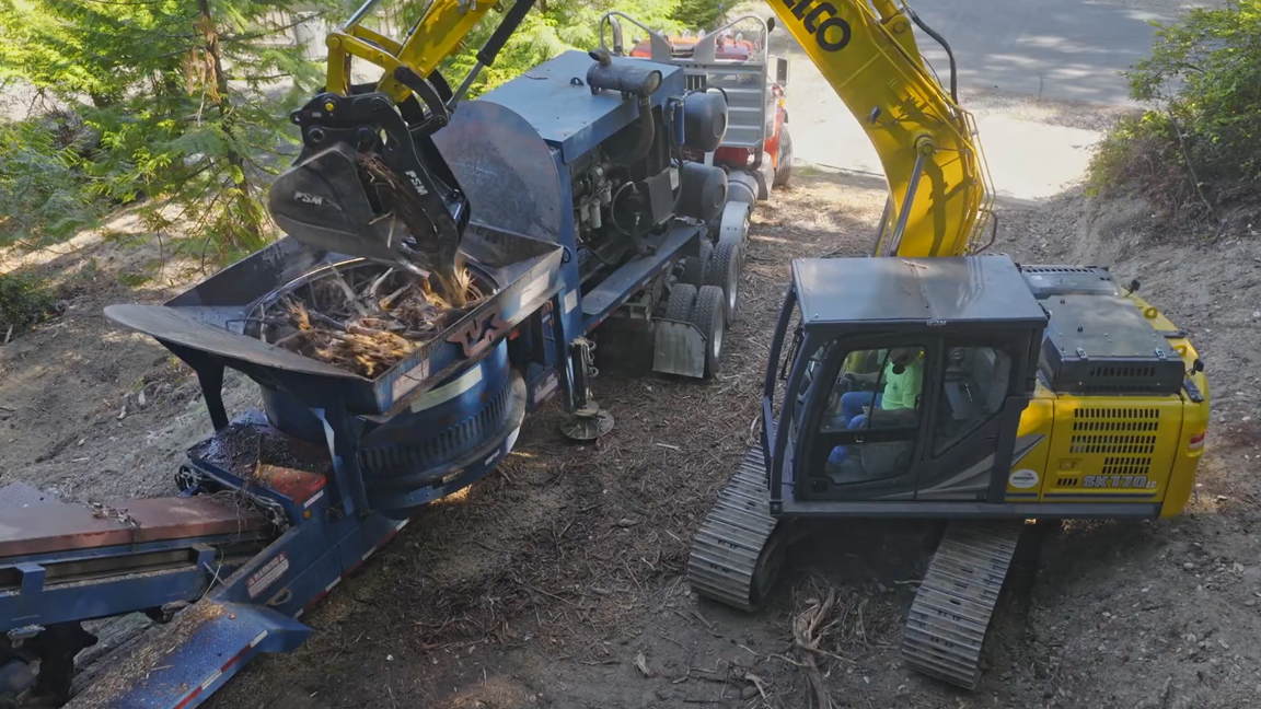 Heavy excavator loading wood waste into industrial chipper