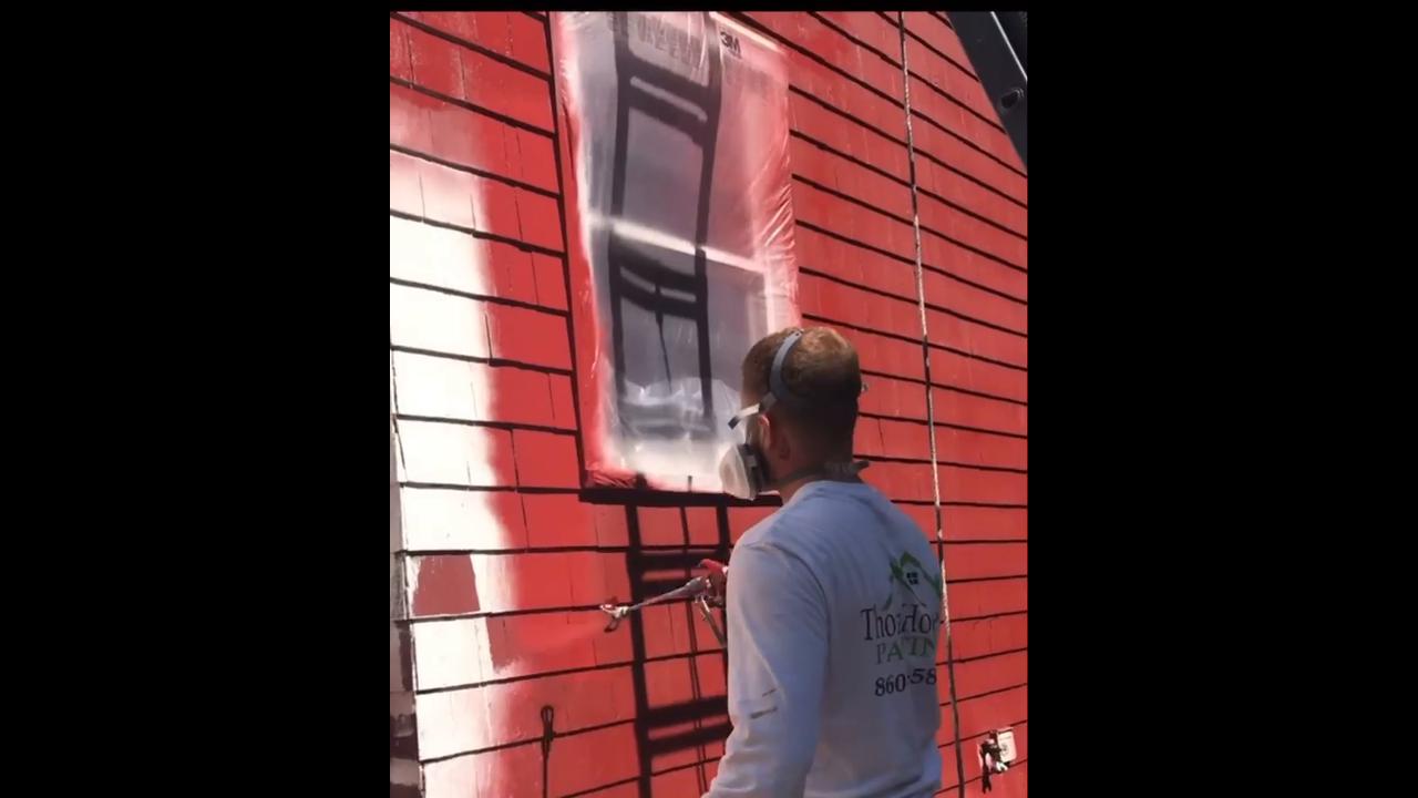 Spray painting red exterior wall around window creating bold modern finish