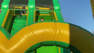 Boy turns sideways and rolls over while sliding down bounce house slide