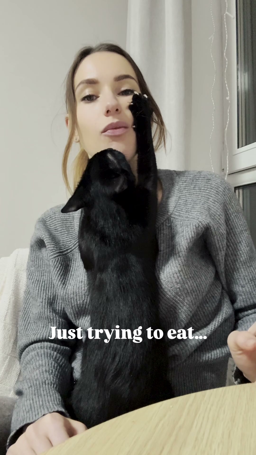 Woman eating a snack with exceptionally clingy black cat