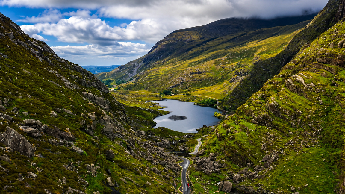 Winding road hidden between massive green mountains