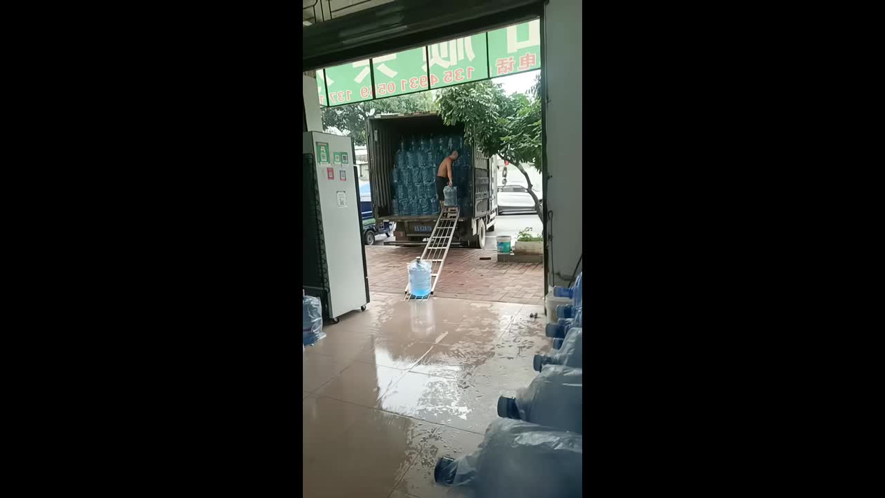 Delivery worker slides water jugs down ramp during unloading in ...