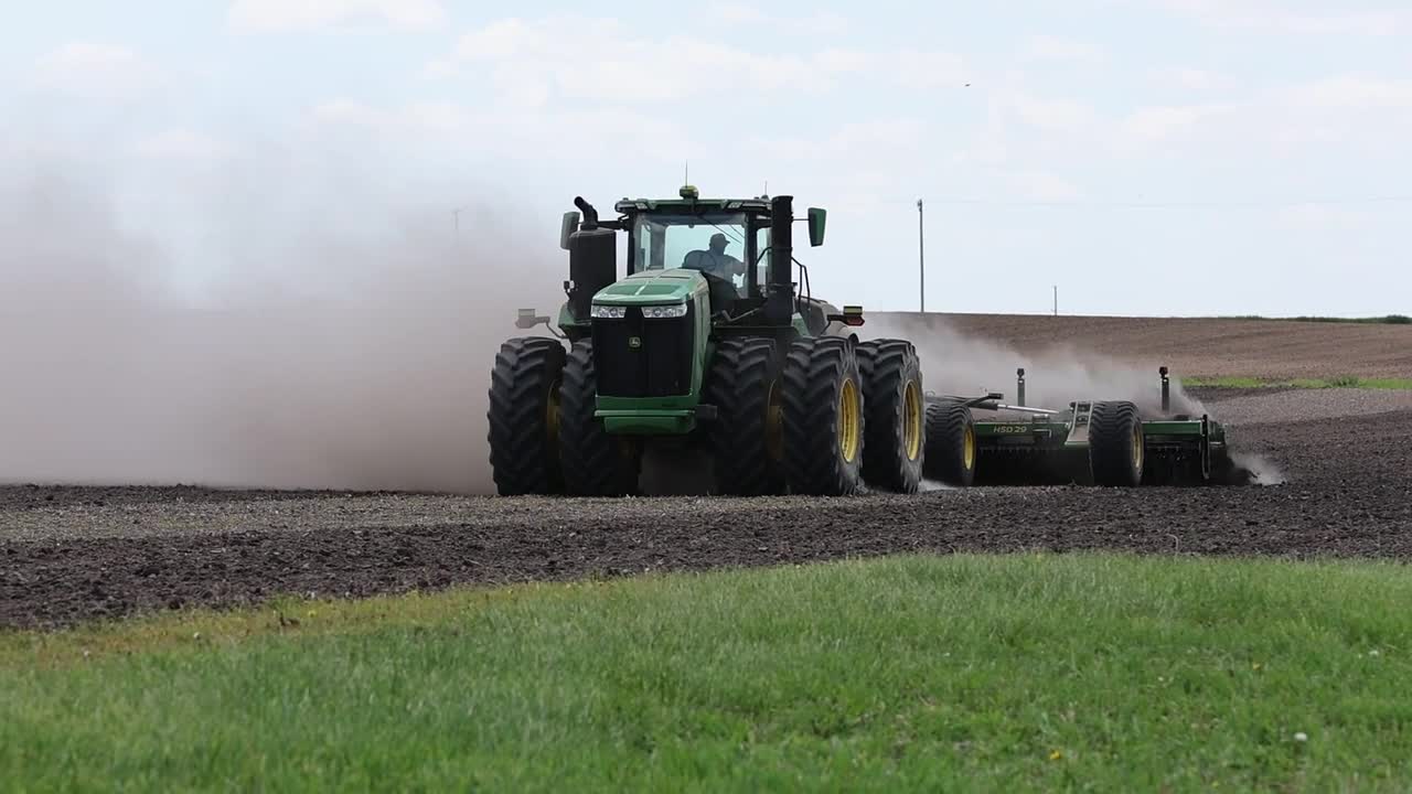 A powerful John Deere tractor moves at high speeds across a sprawling field