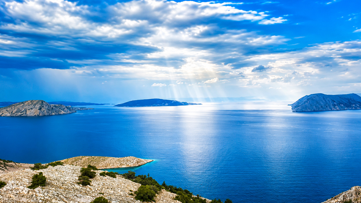 Sunlight breaking through the clouds above the blue sea