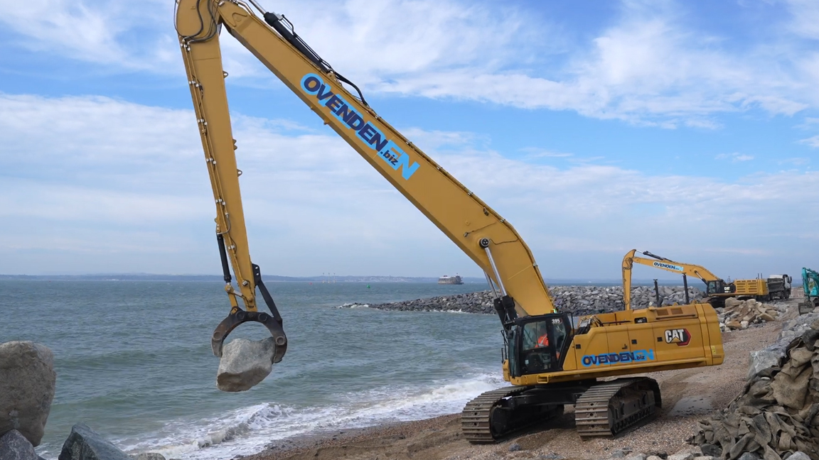 Heavy excavator handling large rocks along coastal breakwater