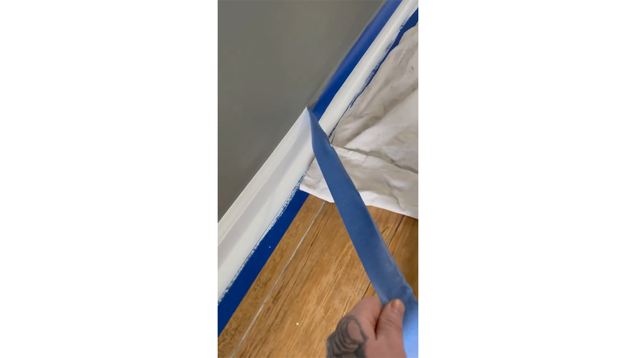 Removing blue painter tape from baseboard creating sharp clean paint line