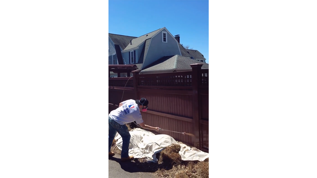 Staining wooden fence with brown coating creating smooth outdoor finish