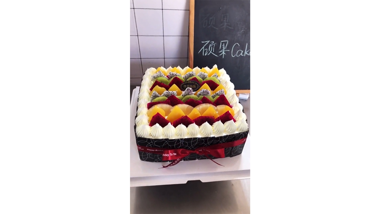Decorating square white cream cake with colorful fruit rows creating ...