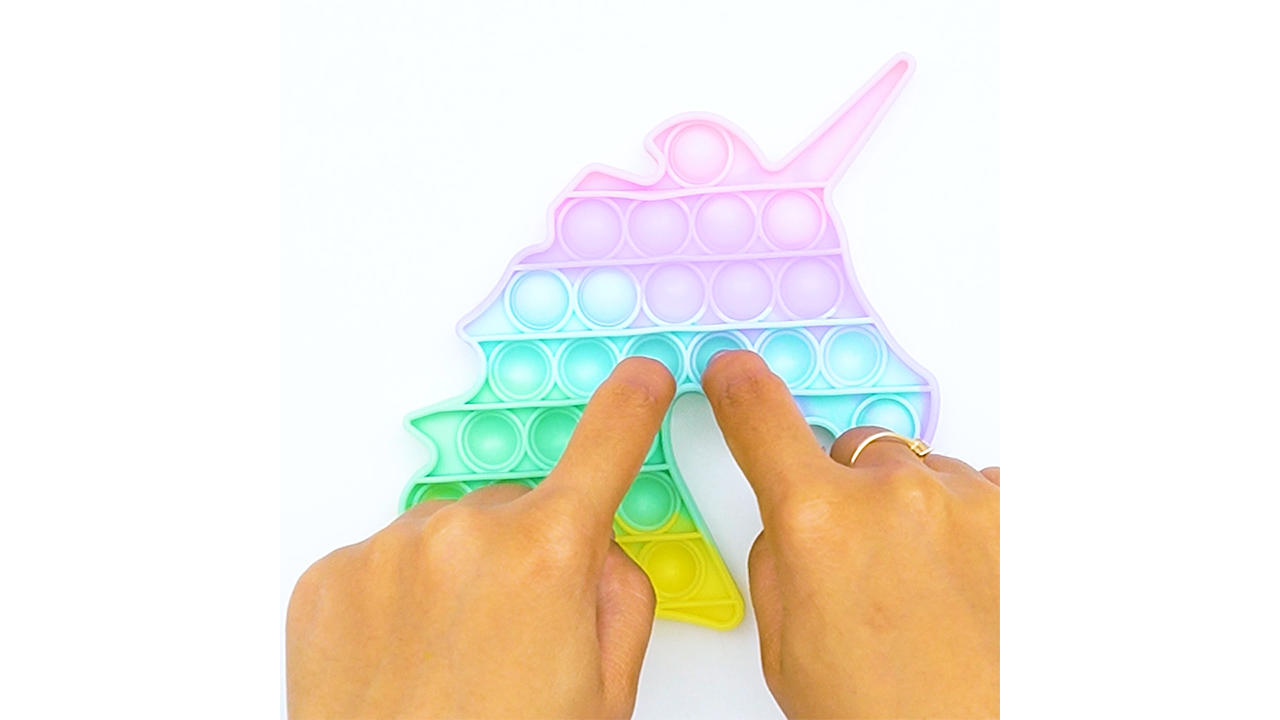 Tapping a unicorn shaped pop it with soft sensory bubbles