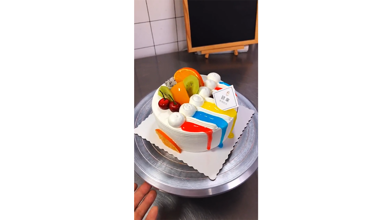 Decorating white cream cake with rainbow icing stripes and fresh fruits ...