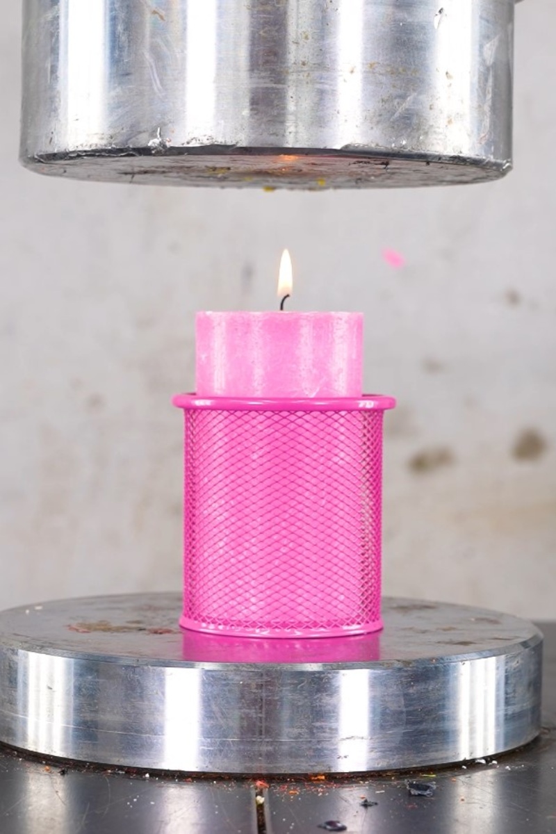 Crushing a candle inside a pink holder under hydraulic press