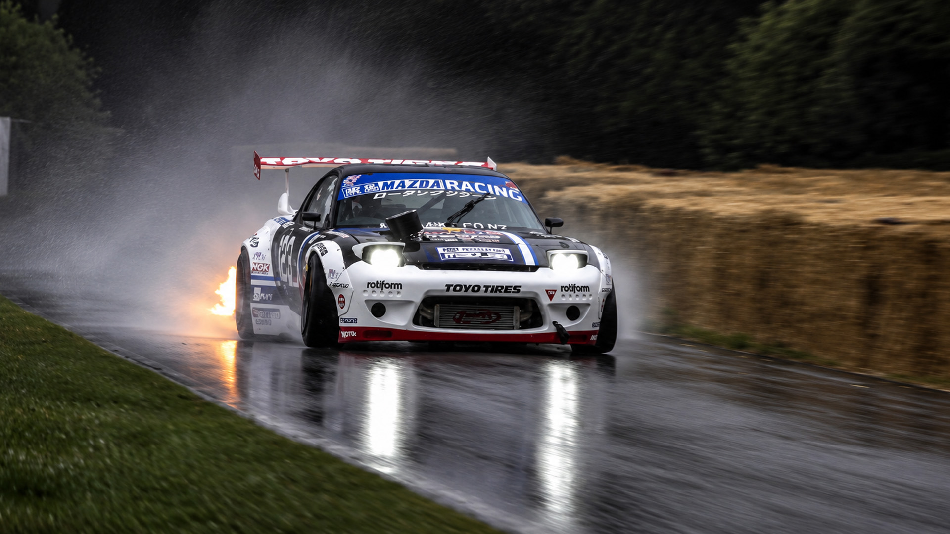Flammen schlagen aus, während der Mazda RX-7 auf nasser Strecke um Grip ...