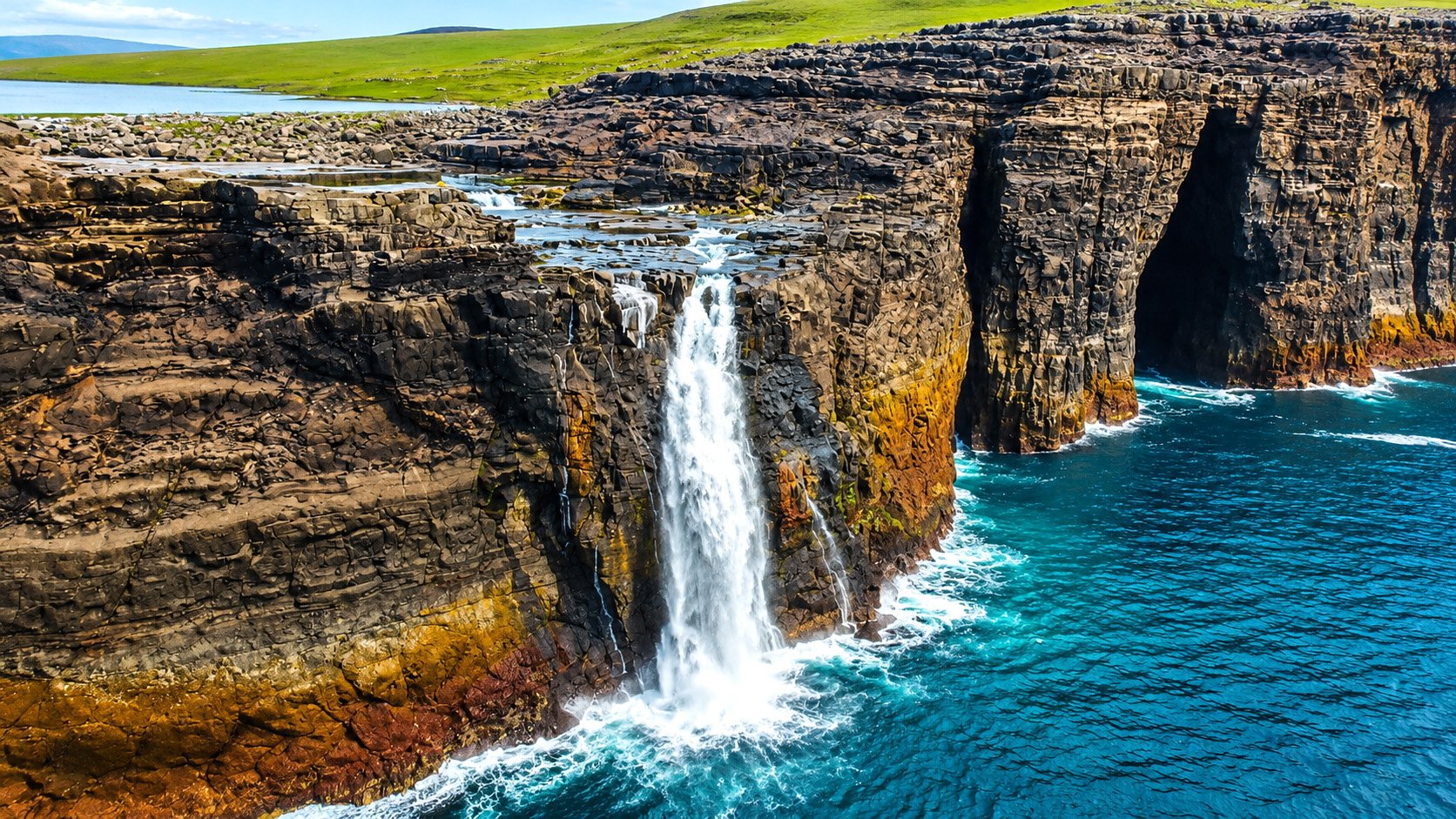 A coastal waterfall falling through rugged cliffs beside the sea