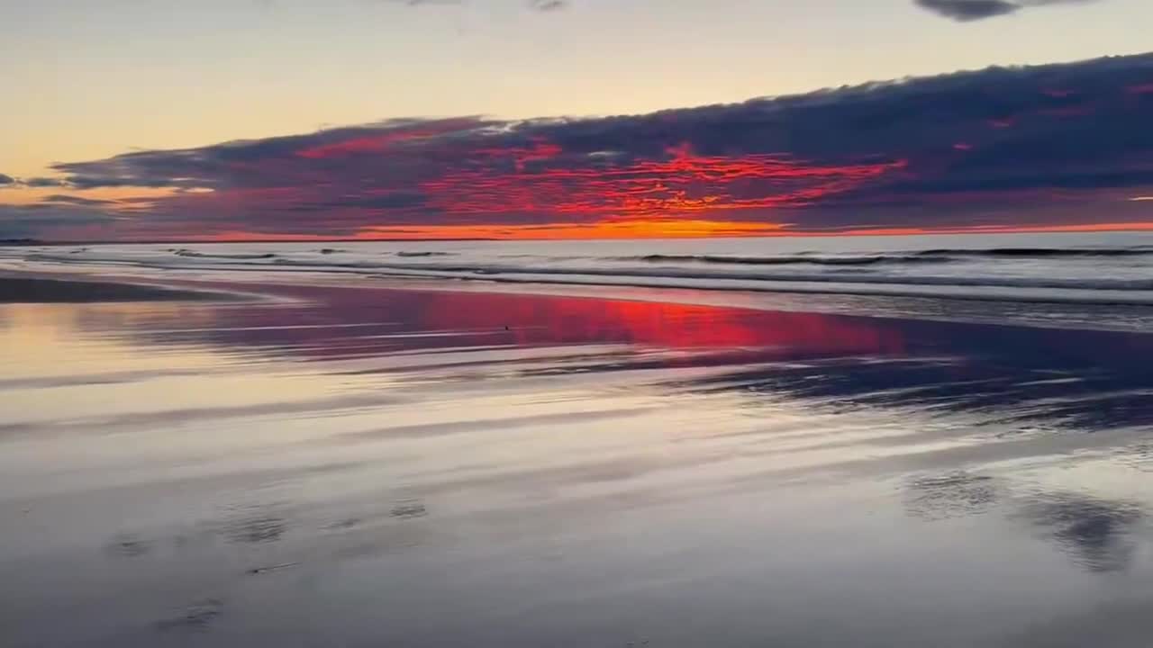 Sunrise over coast of Maine illuminates beach in red and purple